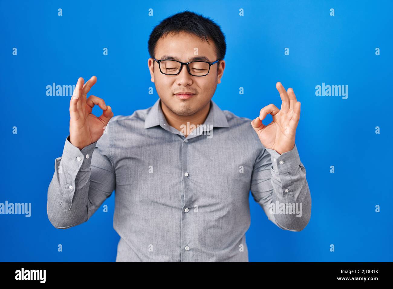 Young chinese man standing over blue background relax and smiling with ...