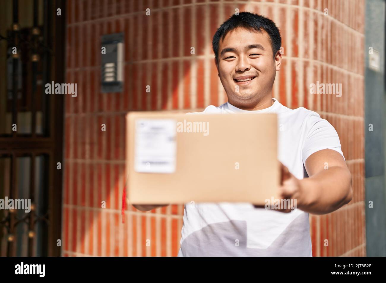 Young chinese man courier holding package at street Stock Photo - Alamy
