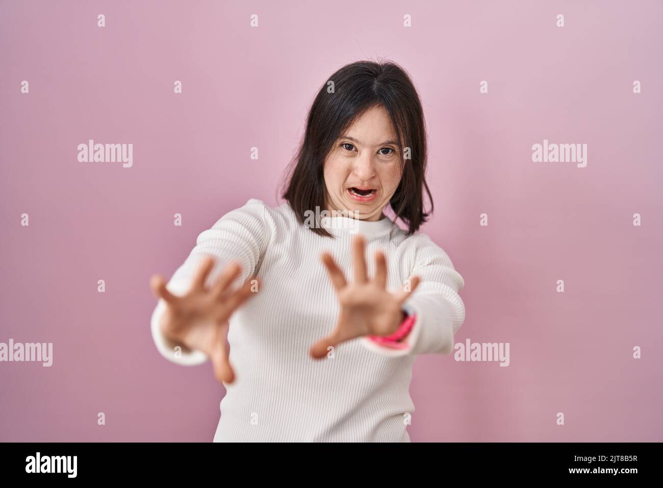 Woman with down syndrome standing over pink background afraid and ...