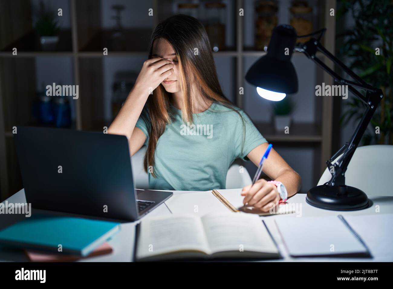 Teenager girl doing homework at home late at night tired rubbing nose ...