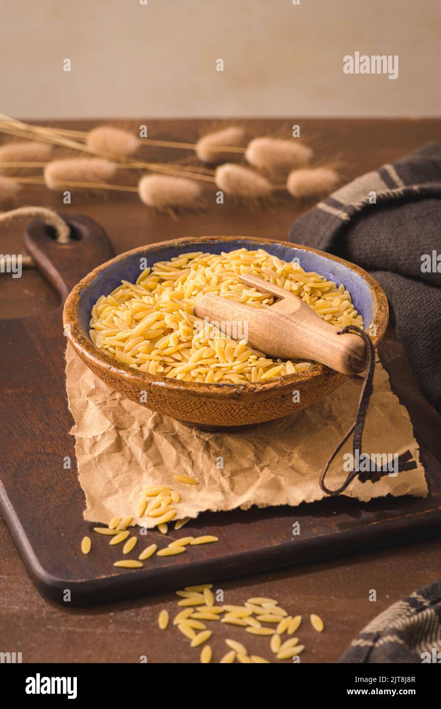 Dry risoni pasta in a ceramic bowl on a rustic kitchen countertop Stock ...