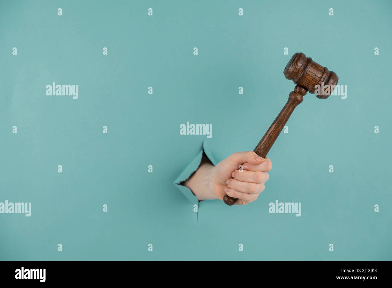 A woman's hand with a wooden judge's gavel sticks out of a hole in a ...