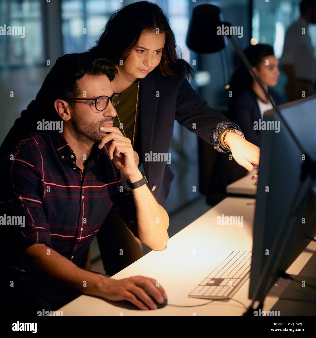 Bright ideas after dark. a businesswoman helping her colleague with his ...