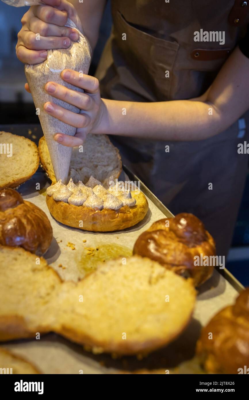 A baker fills brioche cream in a craft bakery. A close-up photo ...
