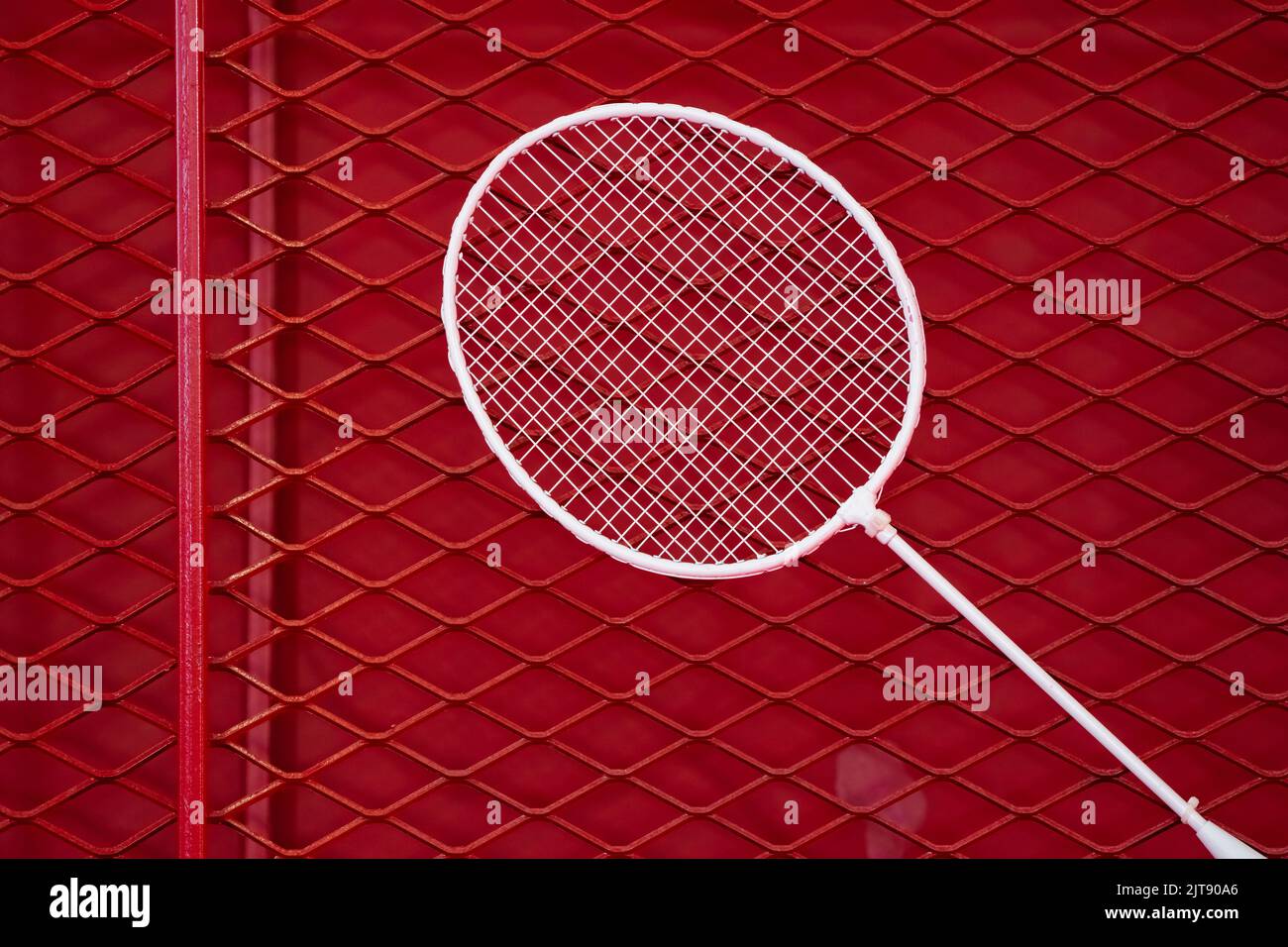 one badminton racket is hung on red grill by a cable tie for display in ...