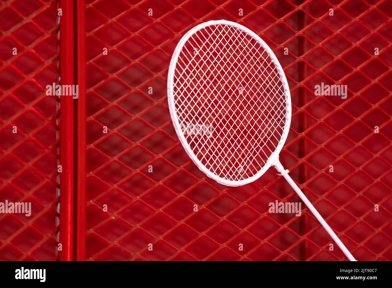 one badminton racket is hung on red grill by a cable tie for display in ...