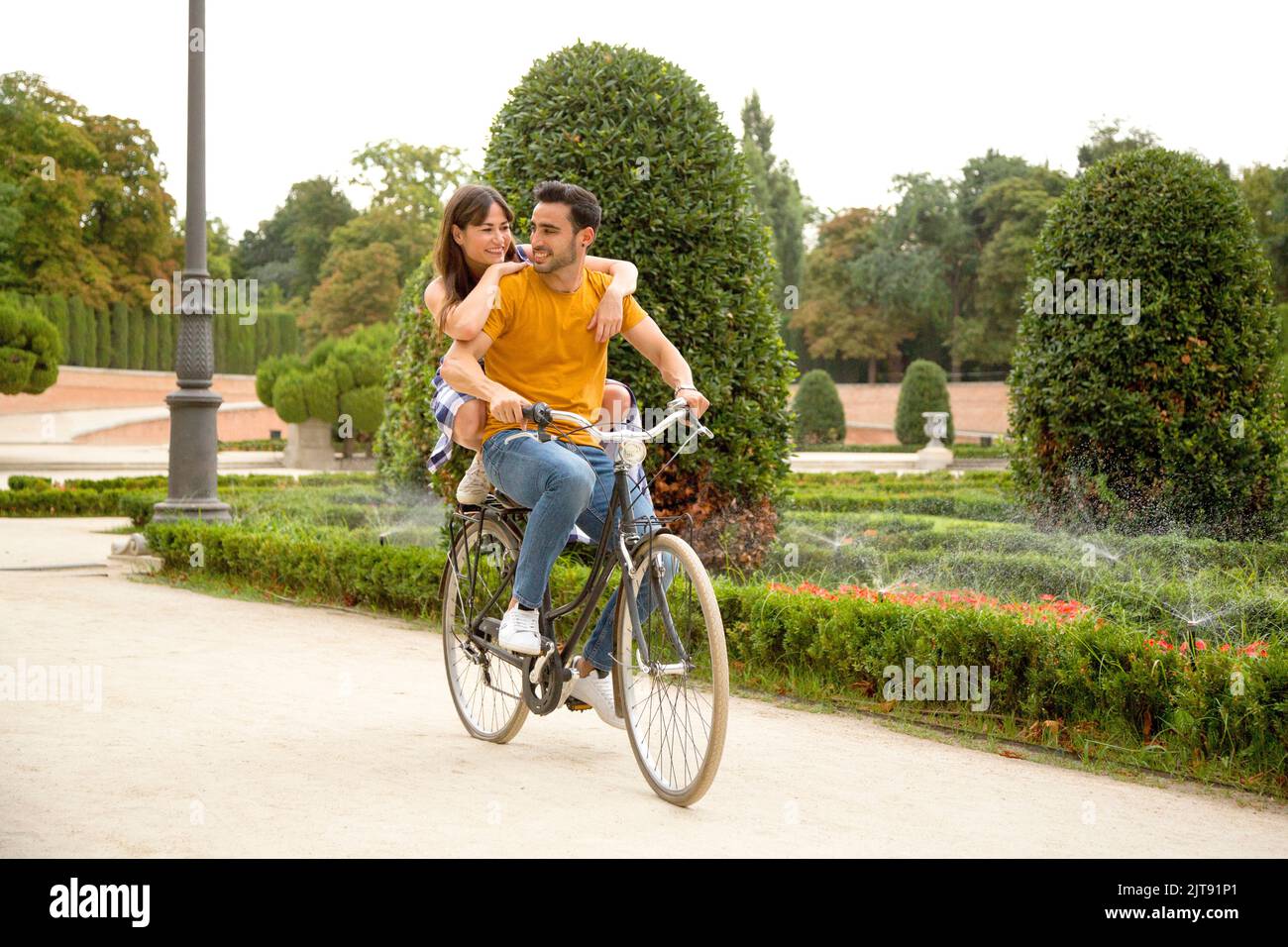 Romantic scene of a caucasian young couple riding a bike in a public ...