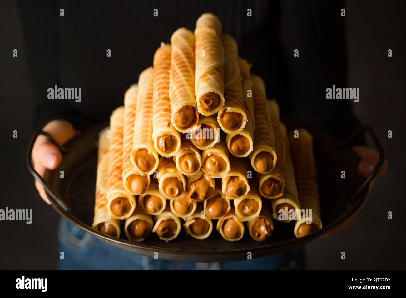 Ruddy crispy tubes with condensed milk on a metal tray in a woman's ...