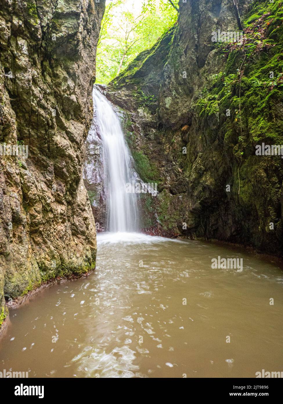 A flowing waterfall falling from rocks surrounded by cliffs Stock Photo ...