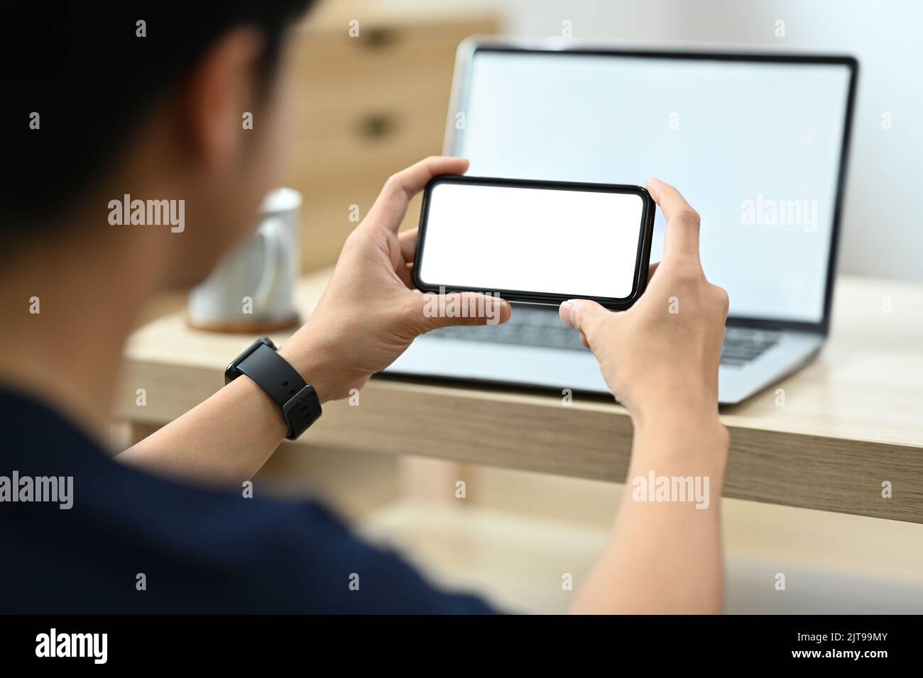 Over shoulder view of man sitting front of laptop and using mobile phone. Blank screen for your ...