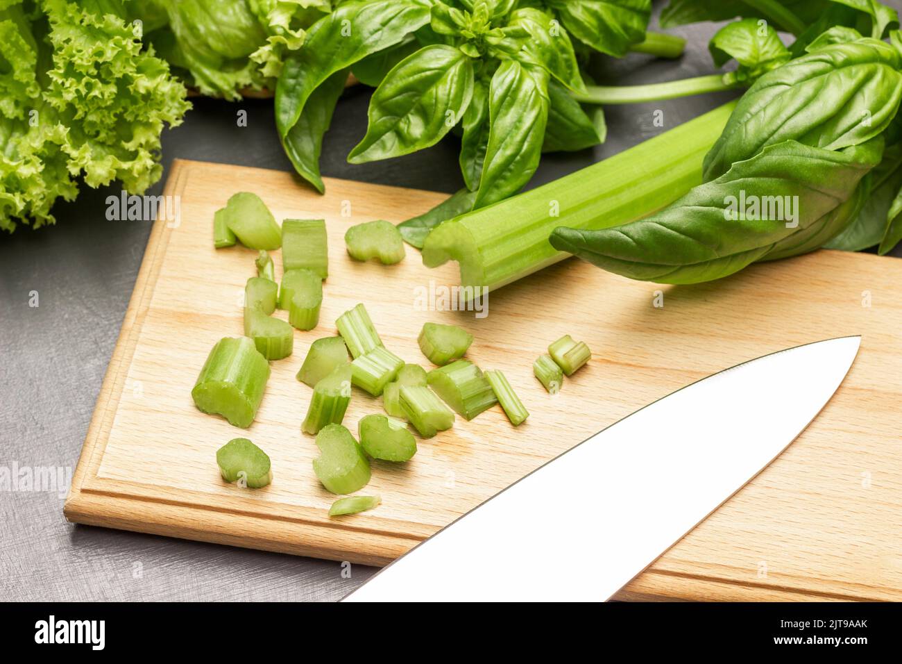 Chopped celery stalks, kitchen knife on cutting board. Basil sprigs and ...