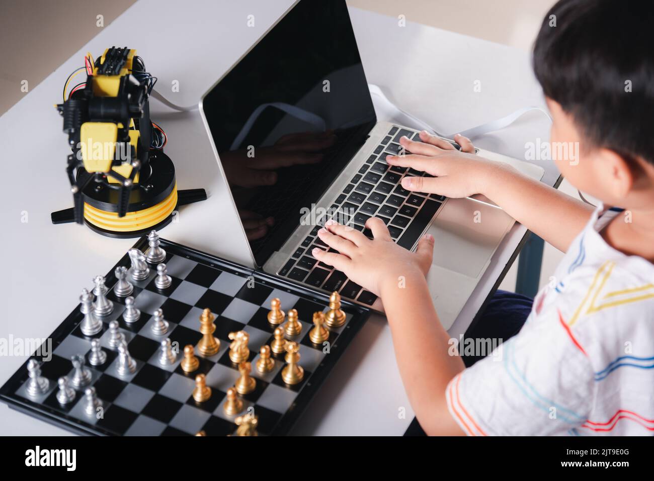 Asian little boy programming code to robot machine arm on laptop for play chess, STEM education ...