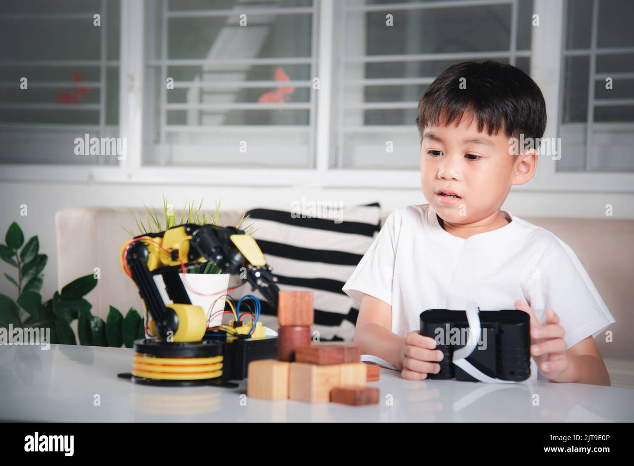 Happy Asian little boy using remote control playing robotic machine arm ...