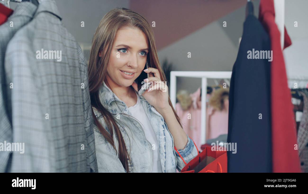 Attractive blond girl choosing fine clothes in modern shop and talking ...