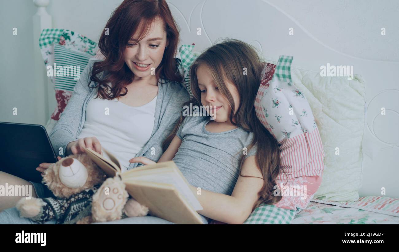 Little cute daughter with young loving mother watching funny pictures ...