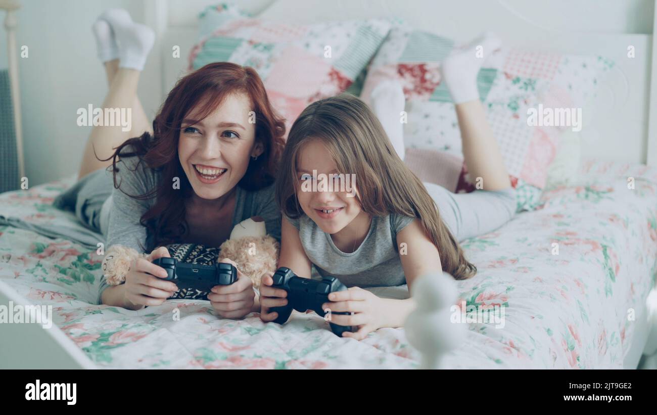 Happy young mother and cute daughter playing computer console games on ...