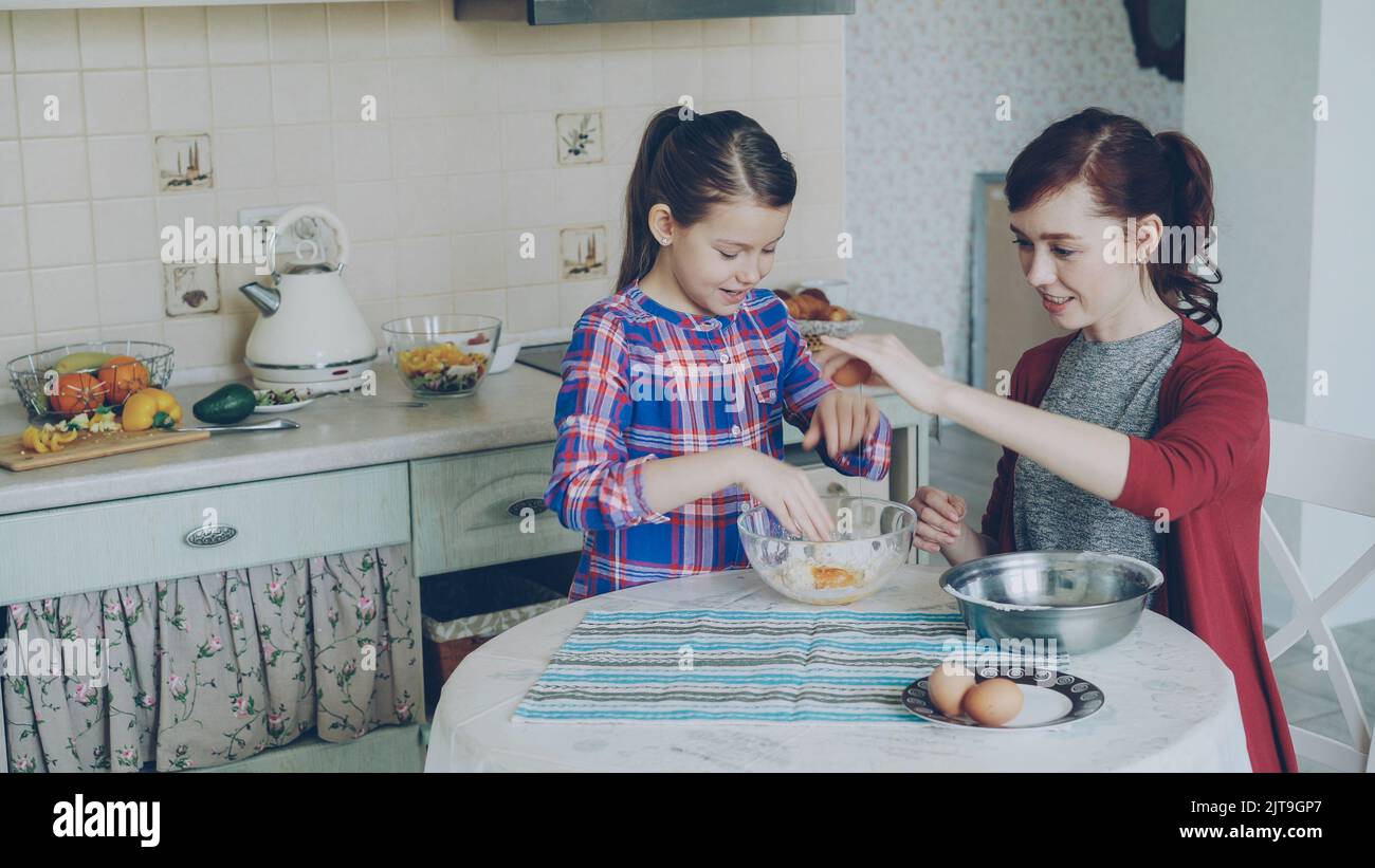 Little cheerful and funny girl helping her mother in the kitchen ...