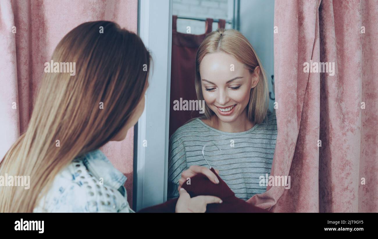 Cheerful young woman is appearing from behind curtain of fitting room ...
