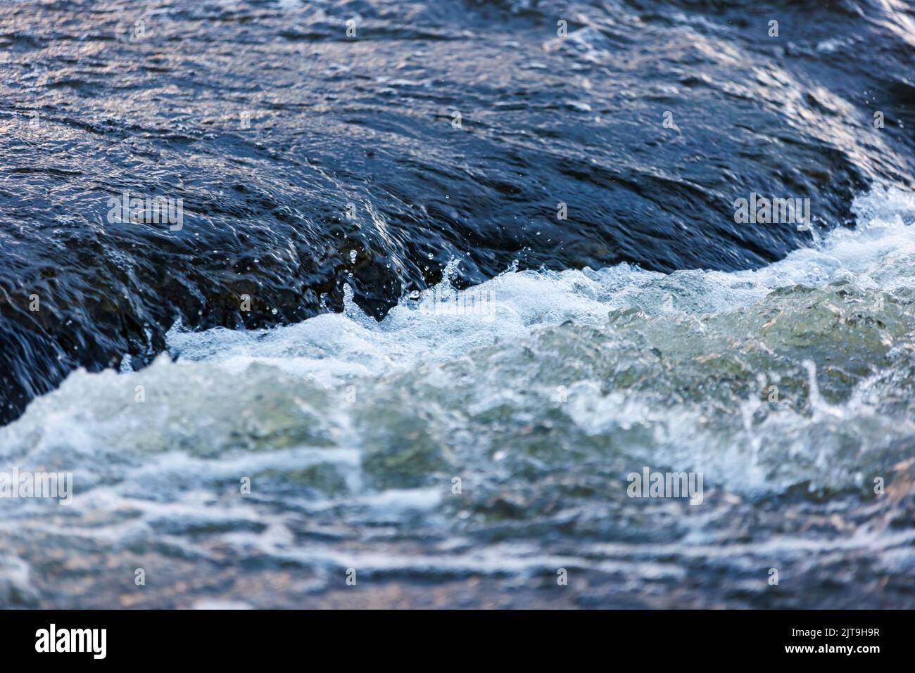 flowing water of a summer river with a small rapid waterfall at evening ...