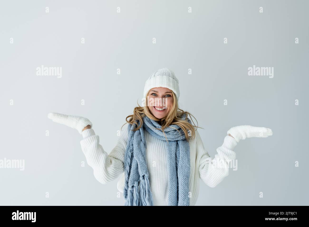 portrait of cheerful woman in winter hat and knitted scarf looking at ...