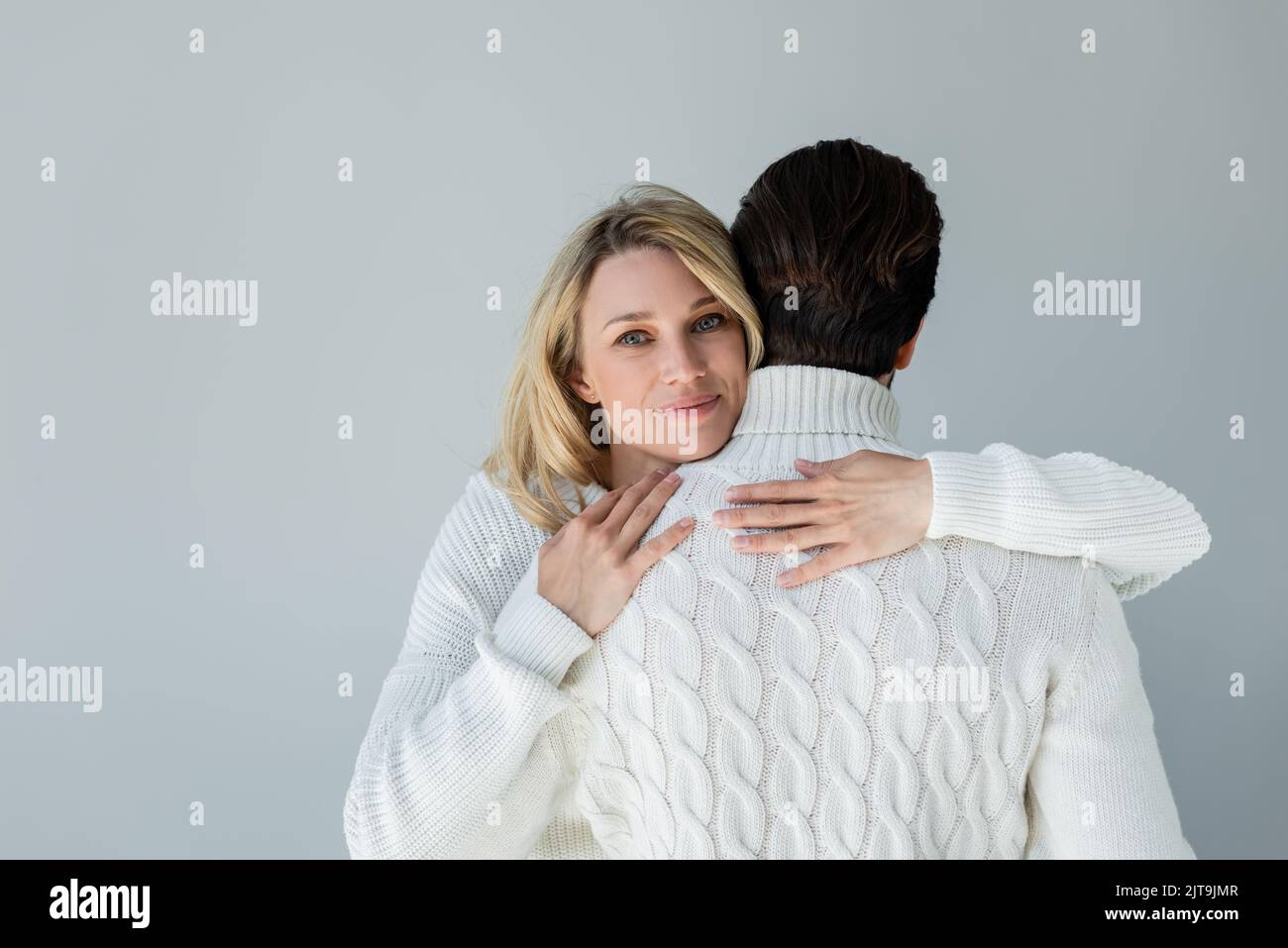 blonde woman in white sweater hugging back of boyfriend and smiling ...