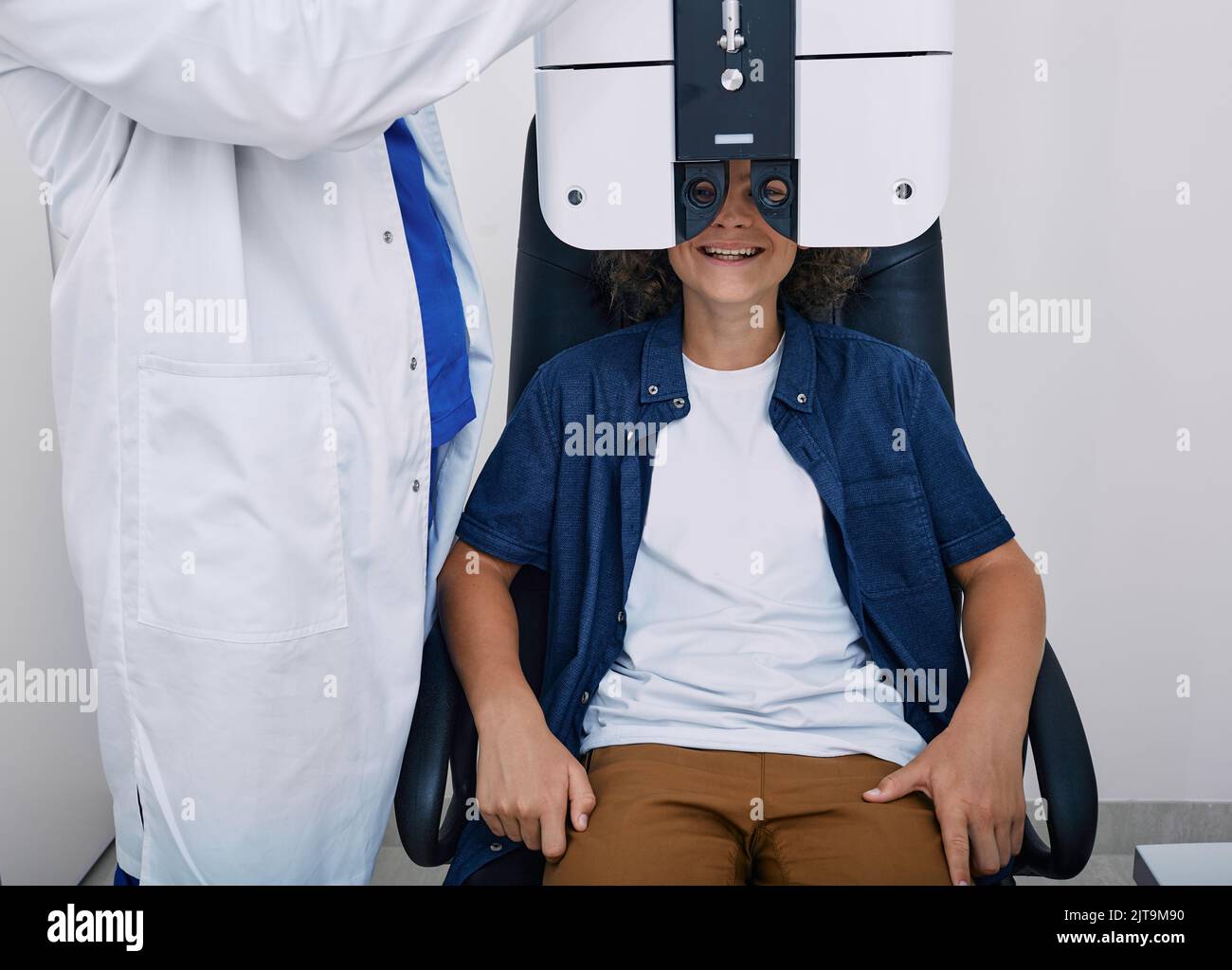 Teenager boy has eye test in ophthalmological clinic using phoropter ...