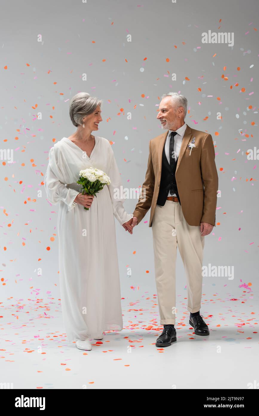 full length of cheerful middle aged groom and happy bride in white ...