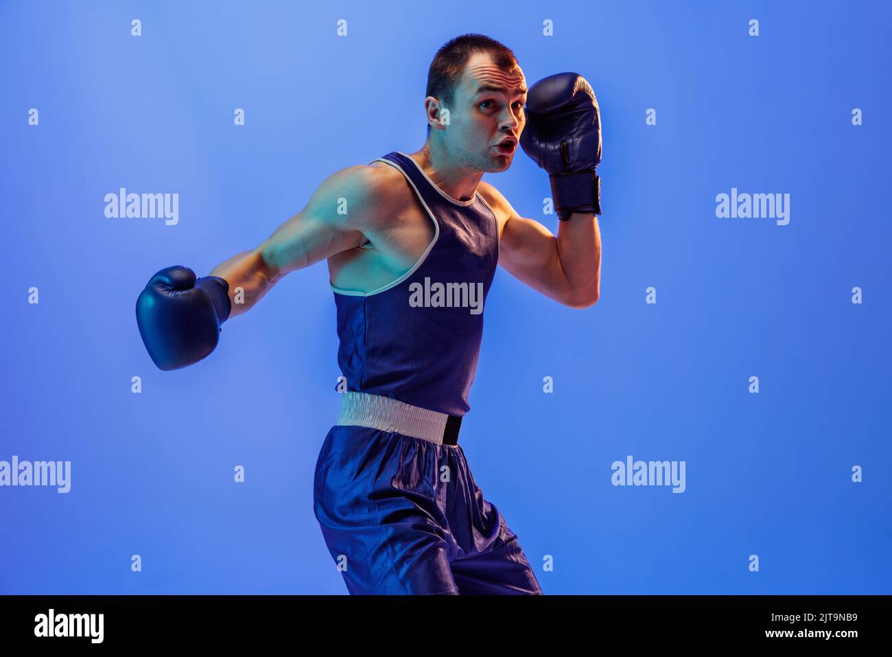 Practicing punch. Muscled man, male boxer in blue uniform and boxing ...