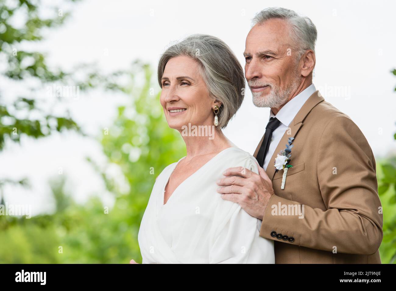 pleased middle aged groom in suit hugging mature bride in white dress ...