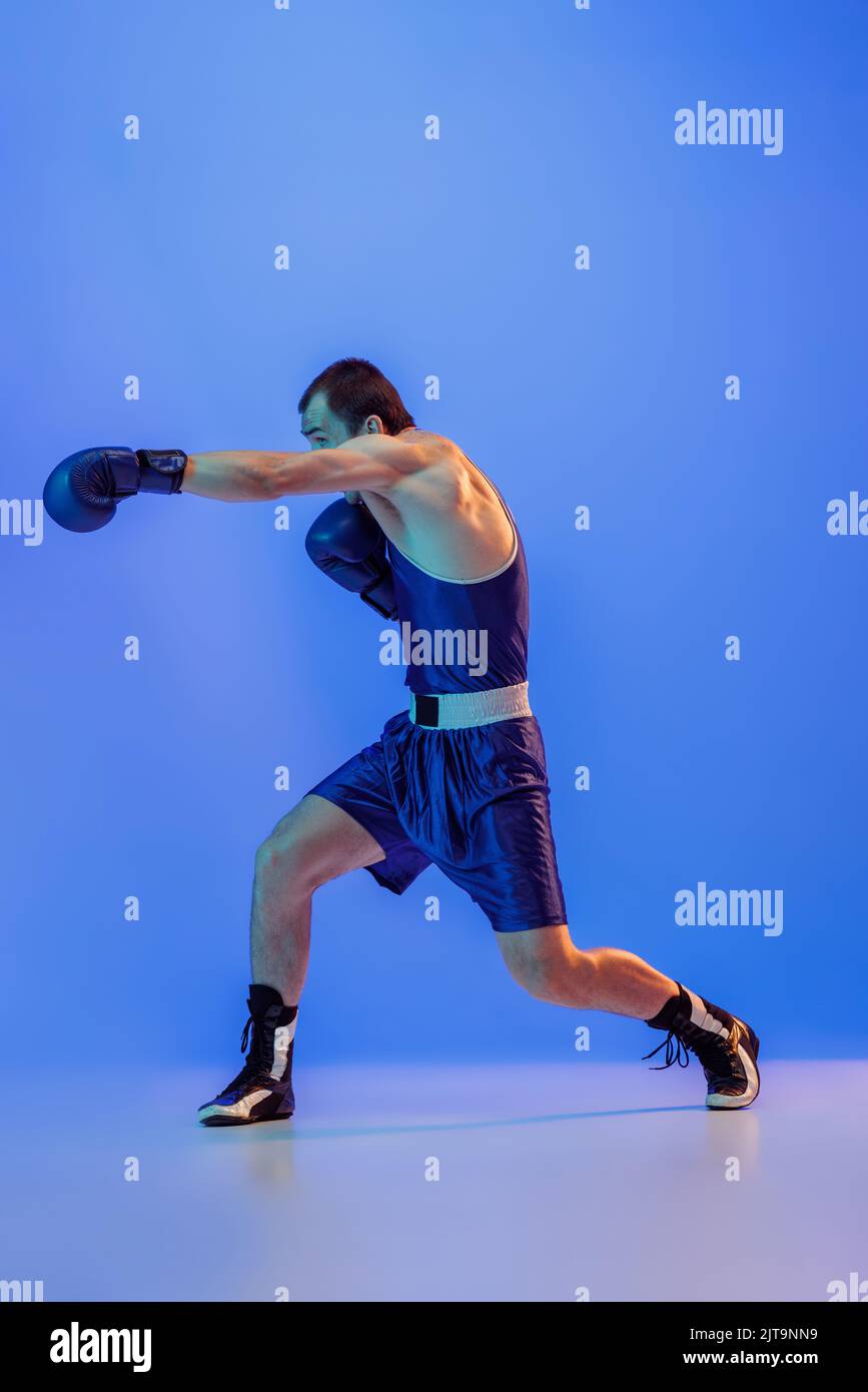 Practicing punch. Muscled man, male boxer in blue uniform and boxing ...