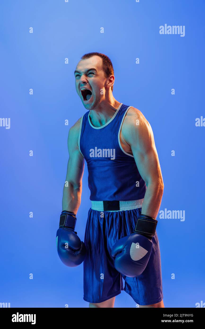 Winner emotions. Male boxer in blue uniform and boxing gloves shouting ...