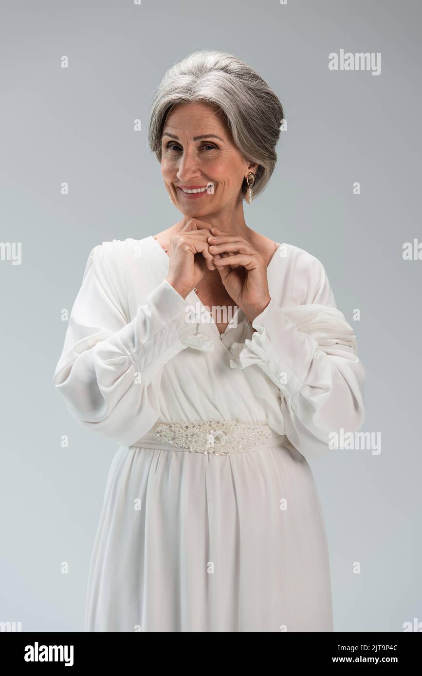 happy middle aged bride in white wedding dress smiling isolated on grey ...
