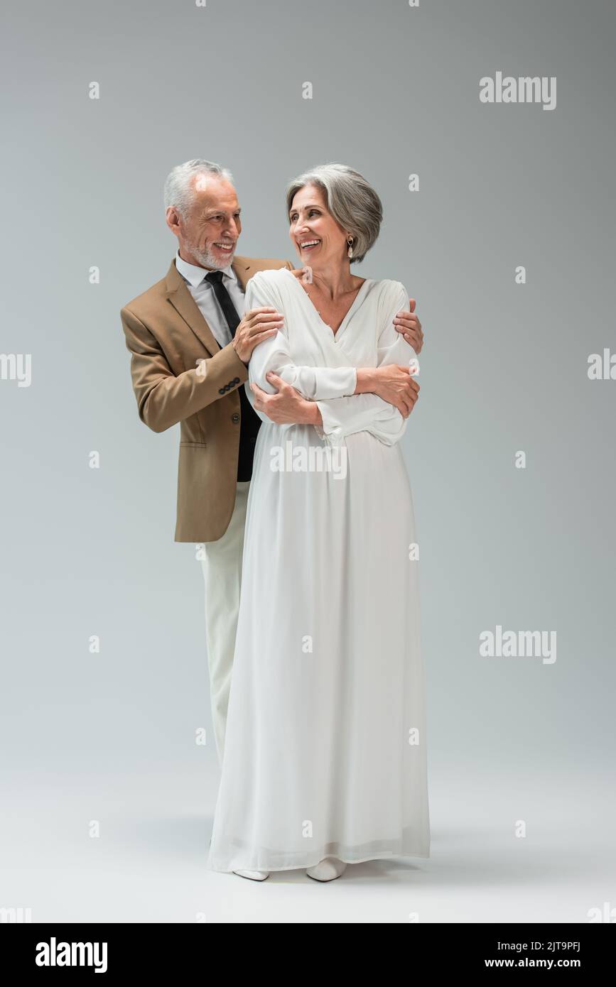 full length of happy middle aged groom hugging cheerful bride in ...