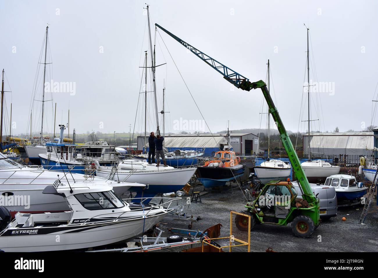 Crane lifting a mast back on to a sailing boat standing in East Llanion ...