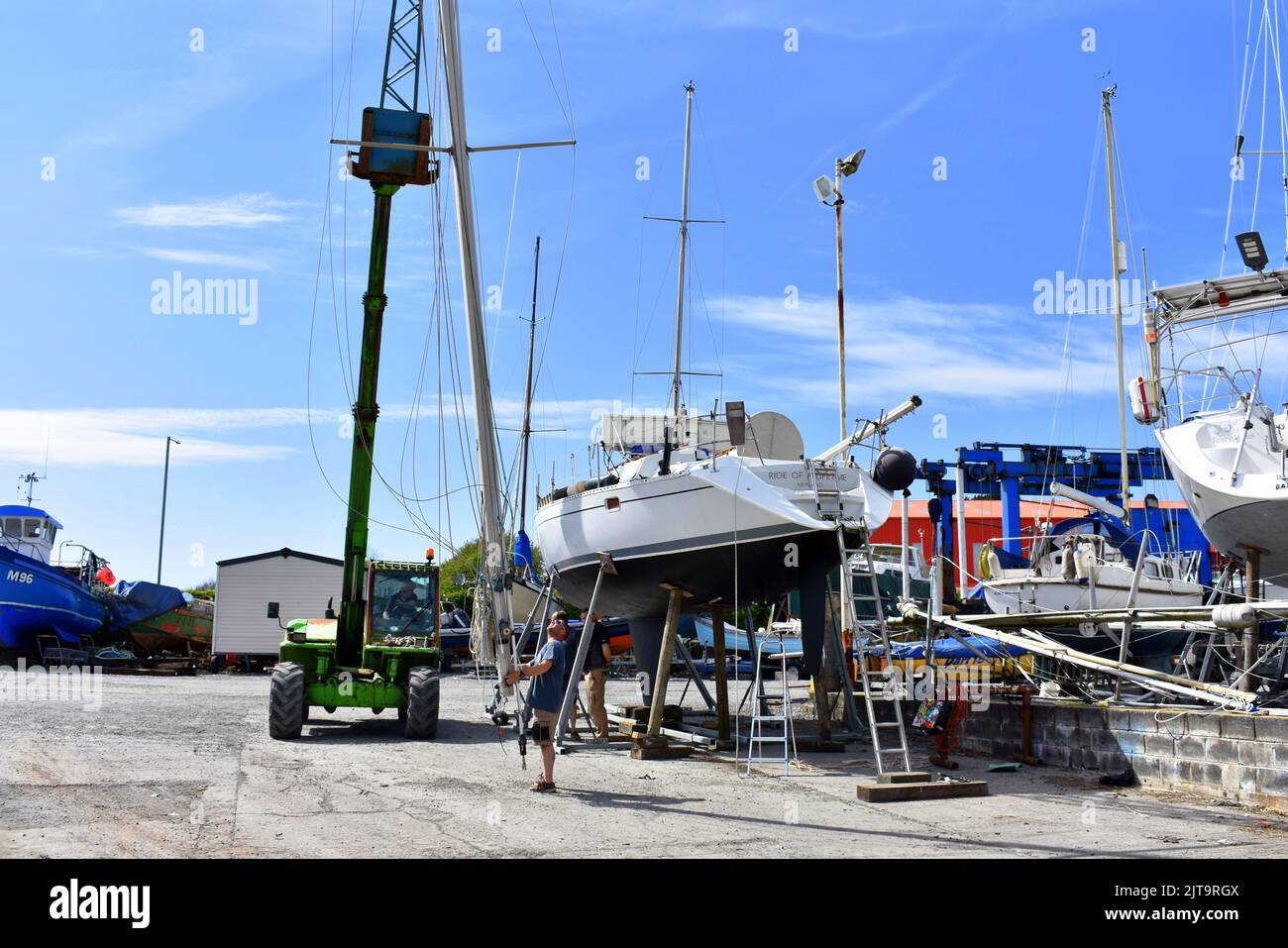 Crane lifting a mast back on to a sailing boat standing in East Llanion boatyard, East Llanion ...