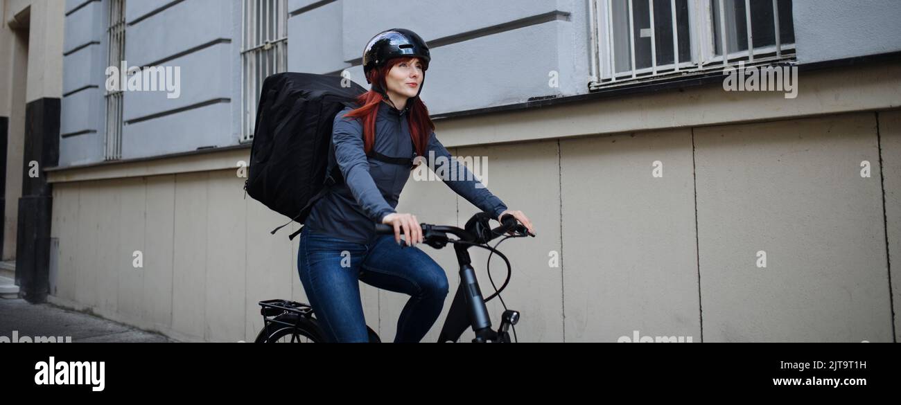 Female courier on bicycle with thermal backpack on way to deliver food ...