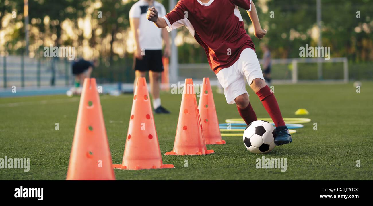School boy running fast and kicking soccer ball on training slalom ...