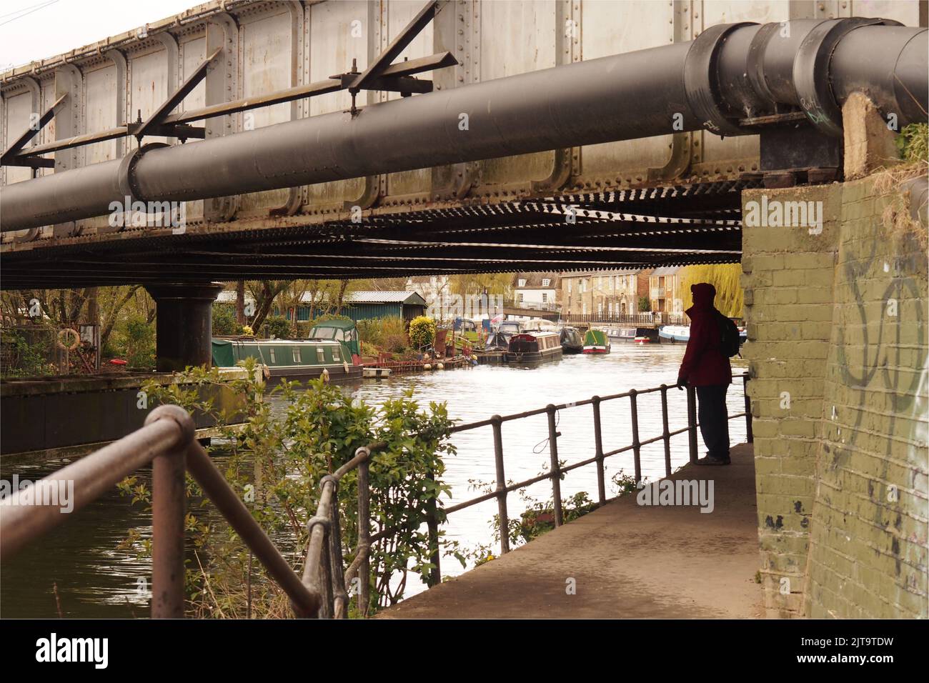 A man 60+ standing under a railway bridge on a canal tow path at Ely ...