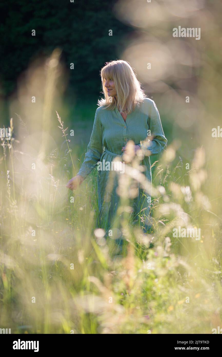 Senior woman in linen dress on walk in meadow in summer, mental health ...
