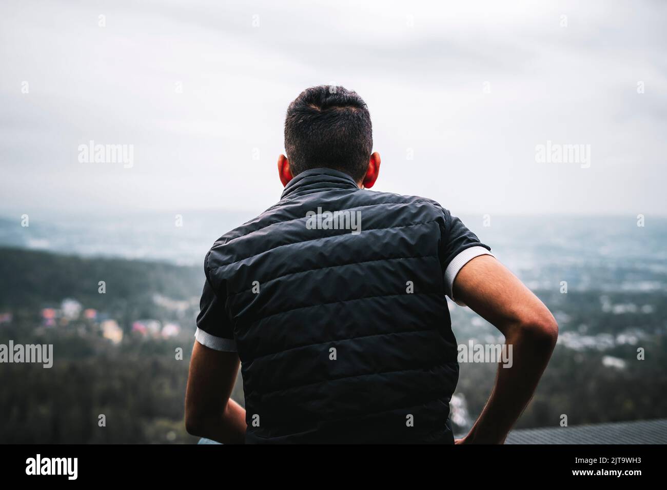 Man sitting with back turned to camera with landscape in the background ...