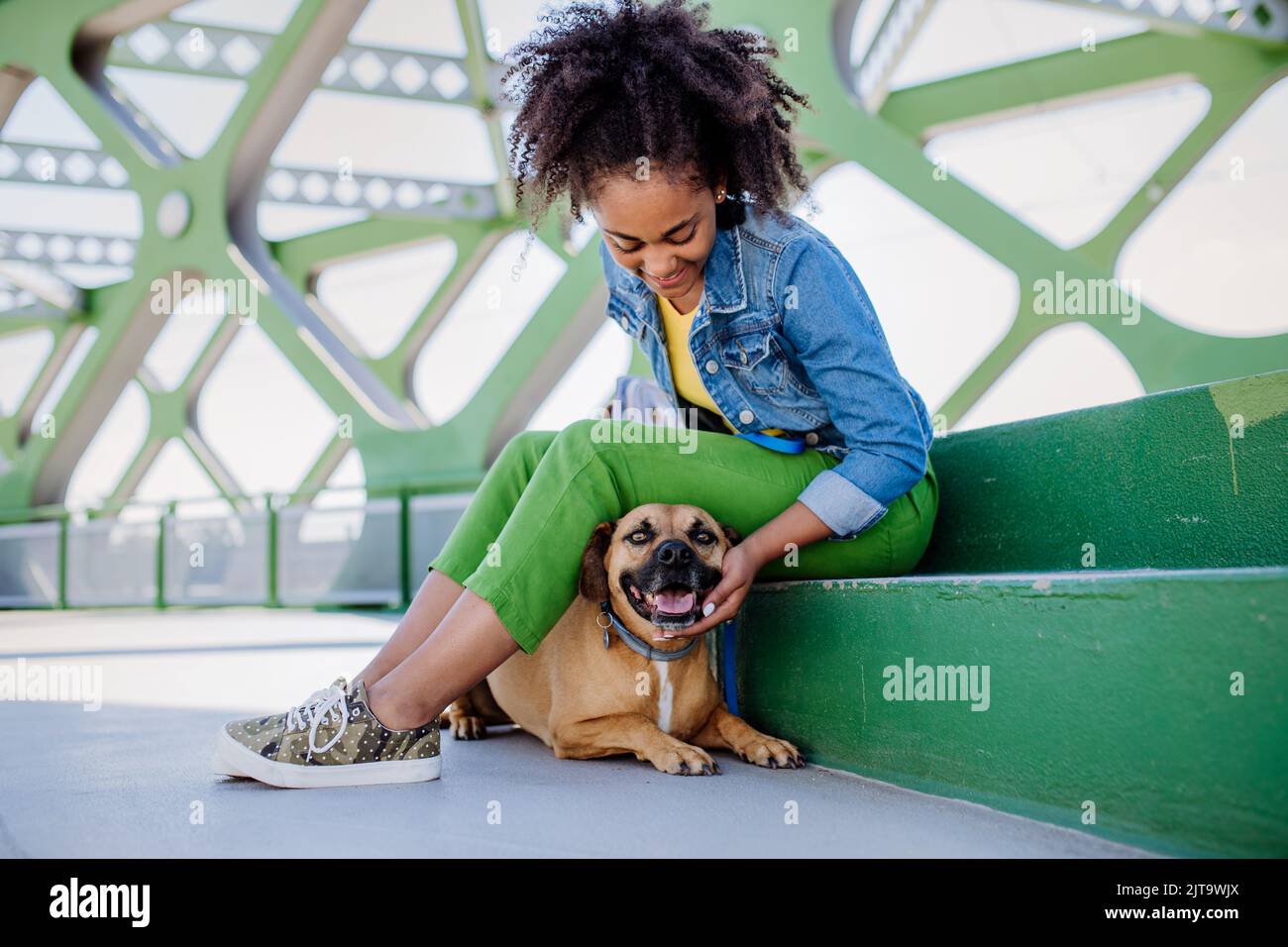 Multiracial girl sitting and resting with her dog outside in the bridge ...