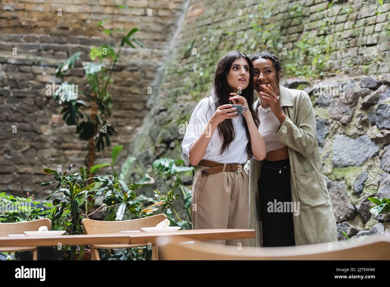 African american woman telling secret to amazed friend with coffee on ...