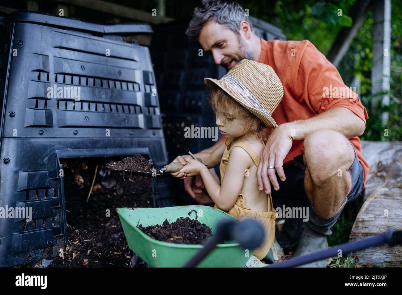 Father with his daughter putting compost out of composter, farmer ...