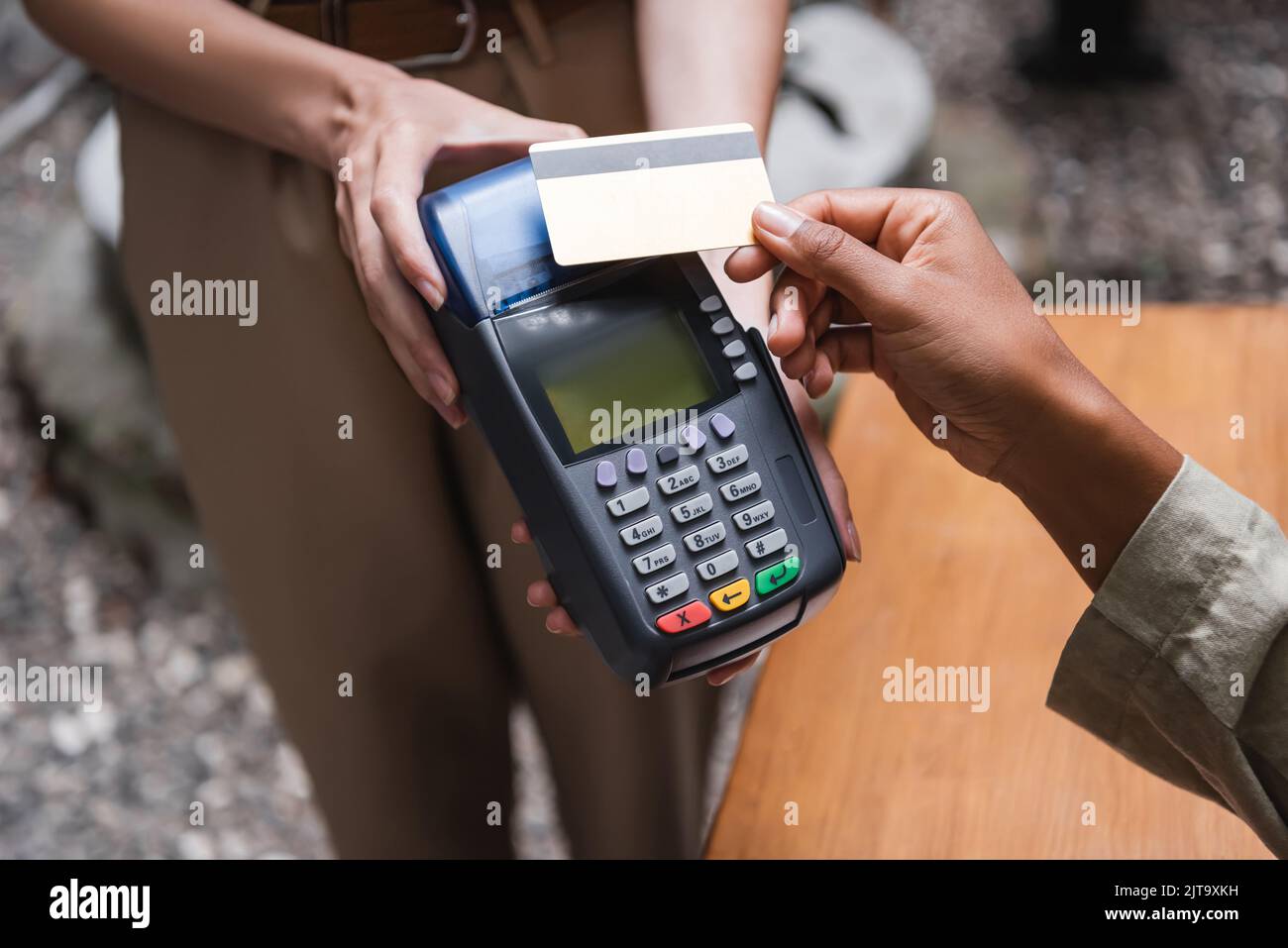 Cropped view of waitress holding payment terminal near african american ...