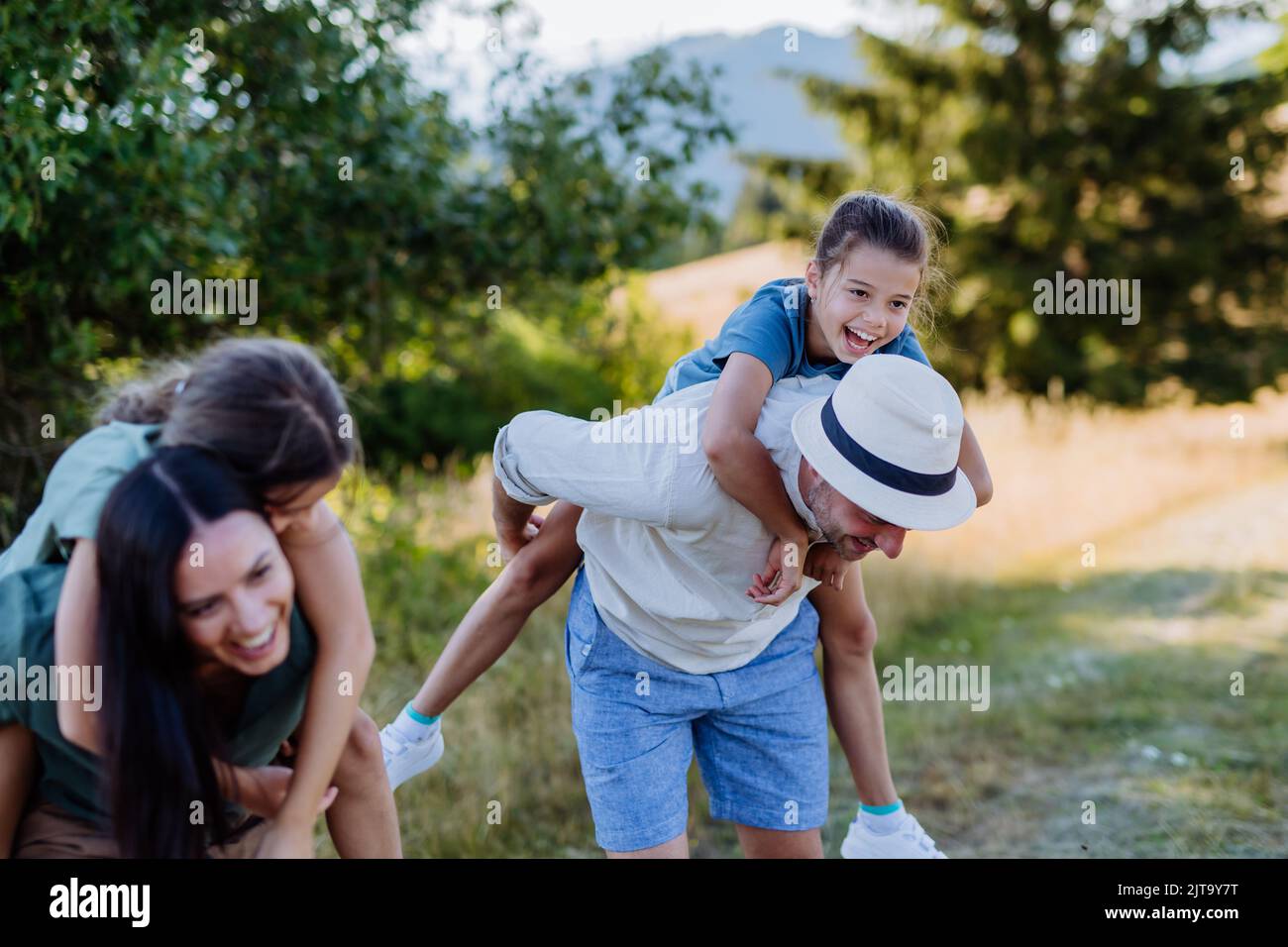 Happy parents giving their children piggyback ride in summer in nature ...