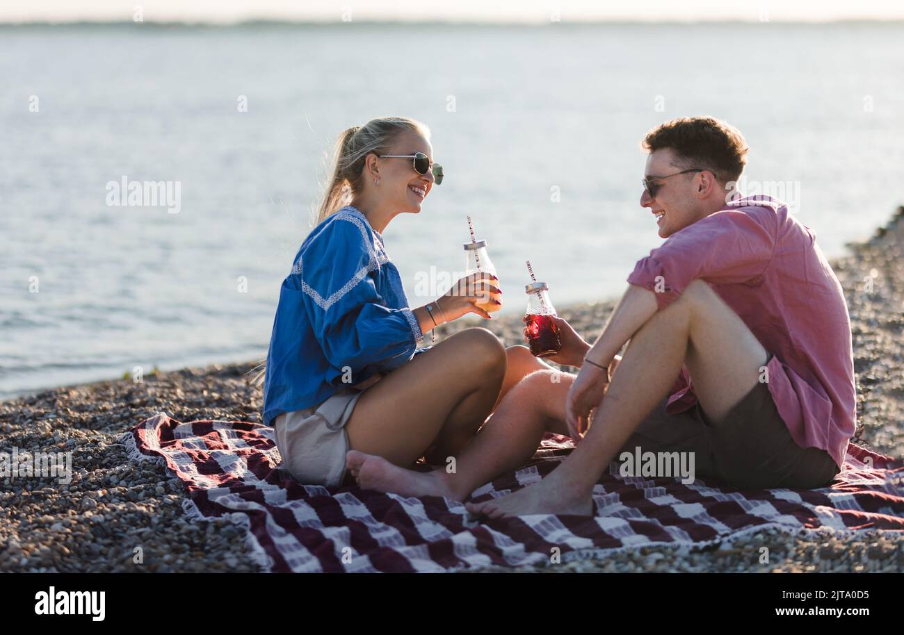 Happy young couple dating together in beach, sitting on a blanket and ...