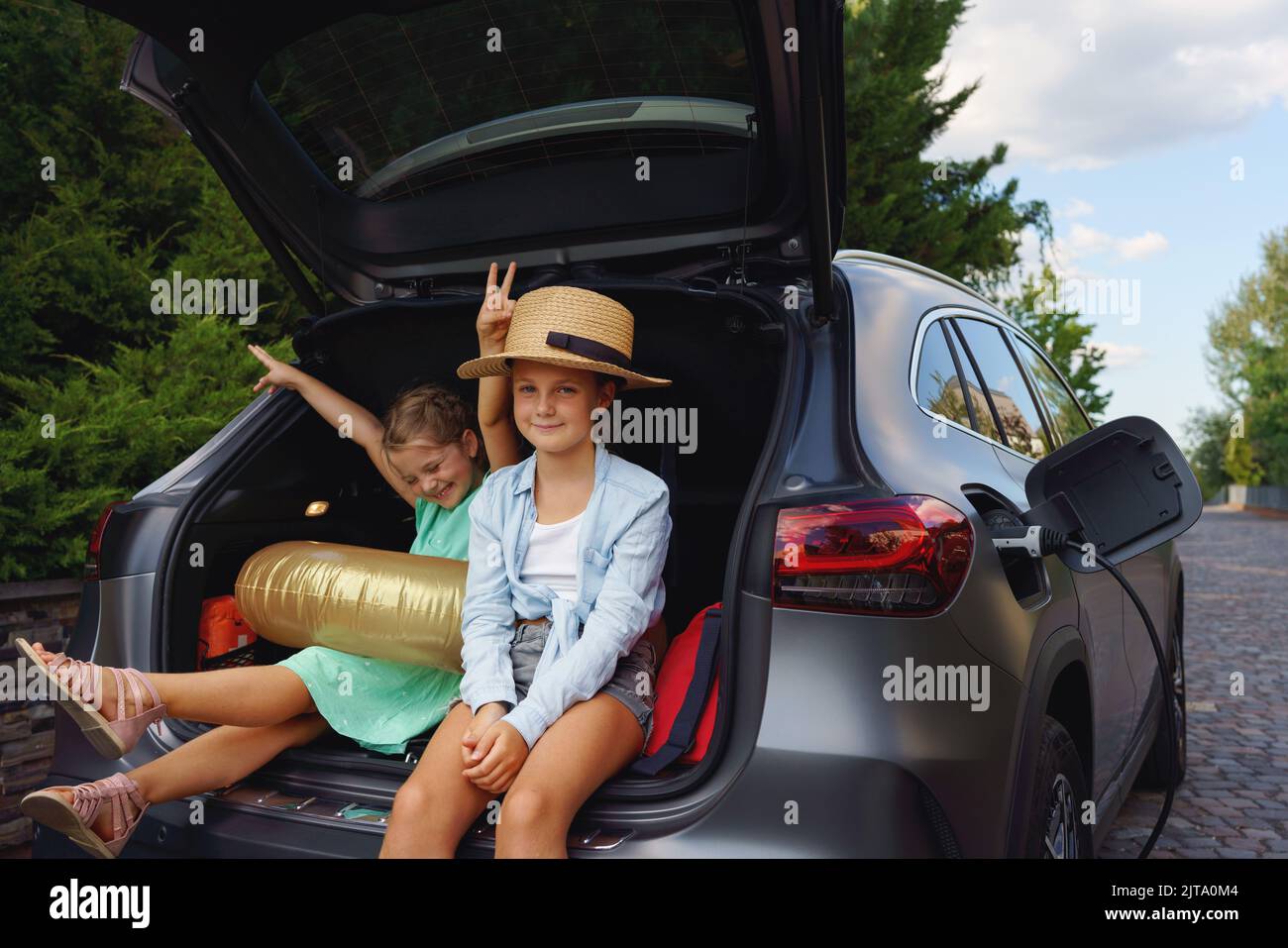 Cute little sisters sitting in trunk while waiting for charging car ...