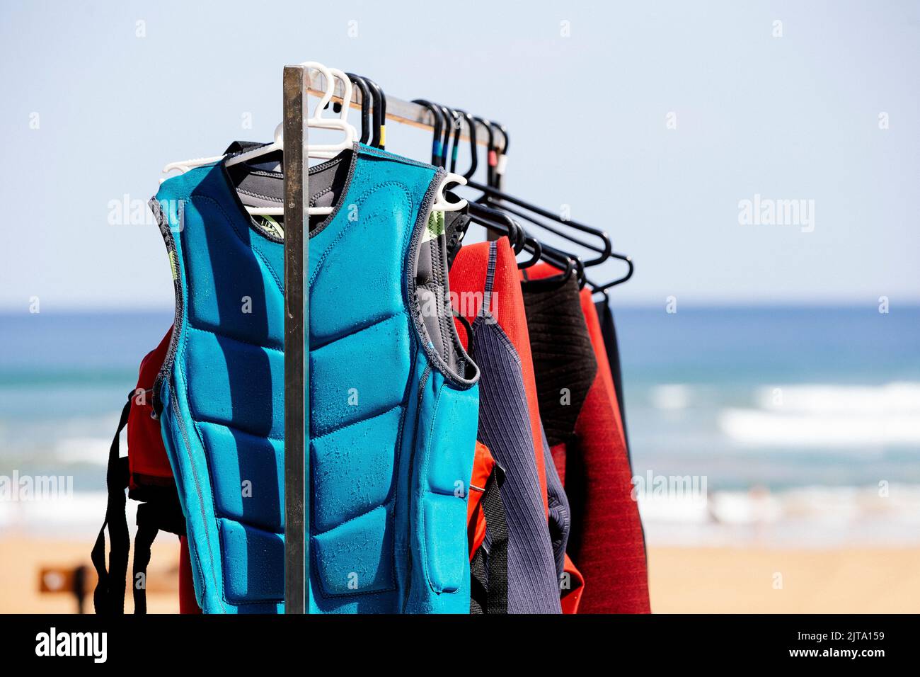 A row of wetsuits hanging on a rack at a surf school Stock Photo - Alamy