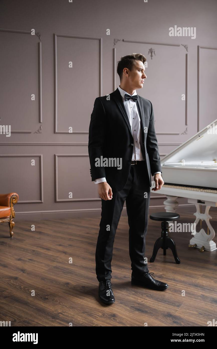 Elegant man in suit standing near piano at home Stock Photo - Alamy