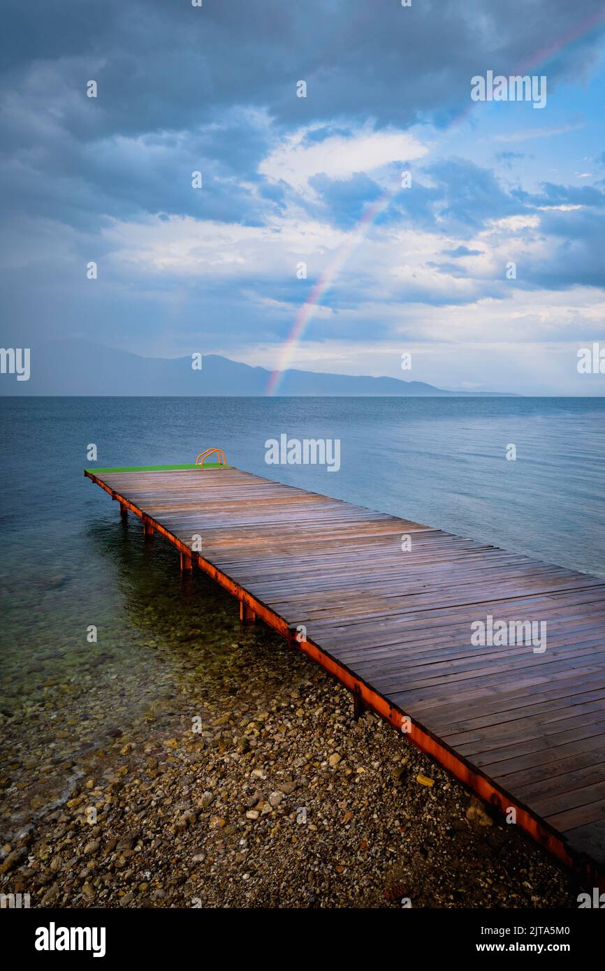 A vertical shot of distant rainbow over the wooden dock after heavy ...